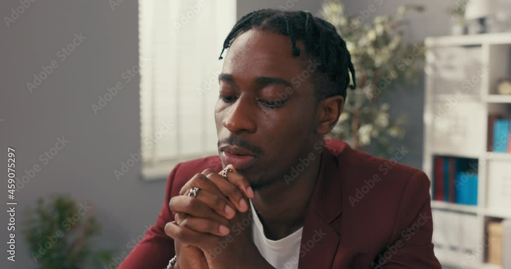 Handsome dark-skinned guy leans against desk with hands bent over ...