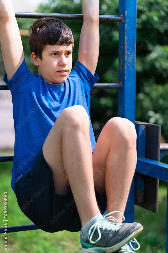 teenage boy exercising outdoors, sports ground in the yard, he hangs on ...