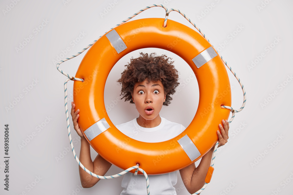 Stunned curly haired young woman scared to swim looks through inflated ...