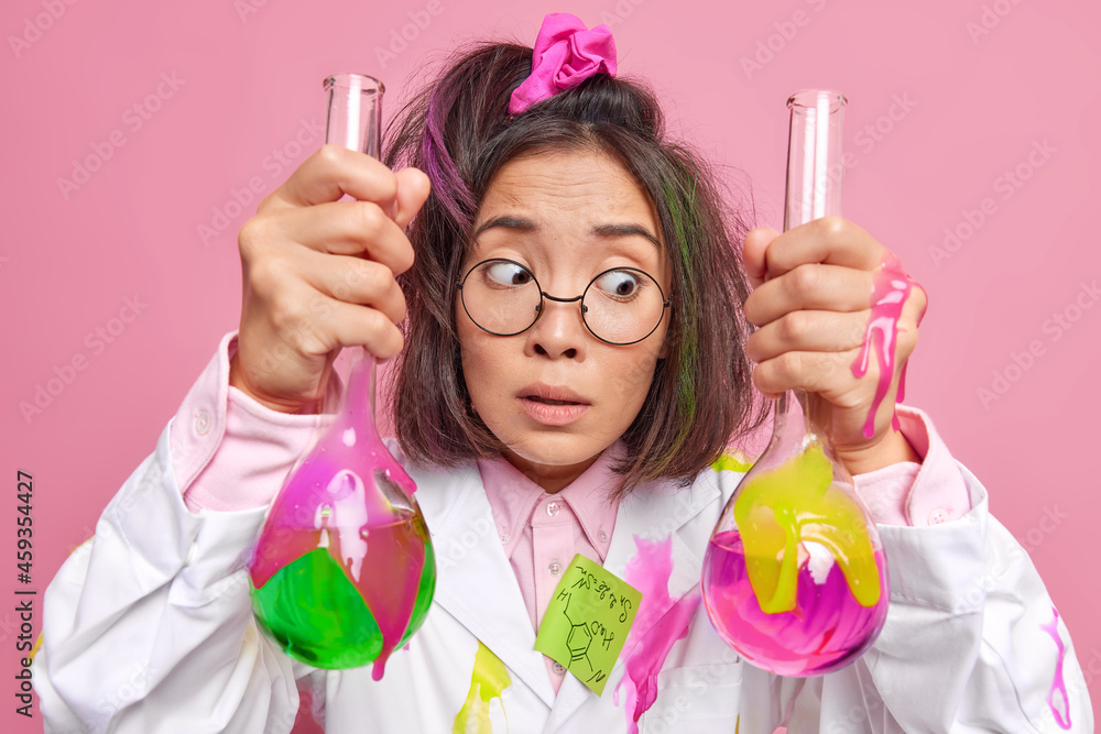 Worried Asian woman holds two glass beakers with liquid samples has ...