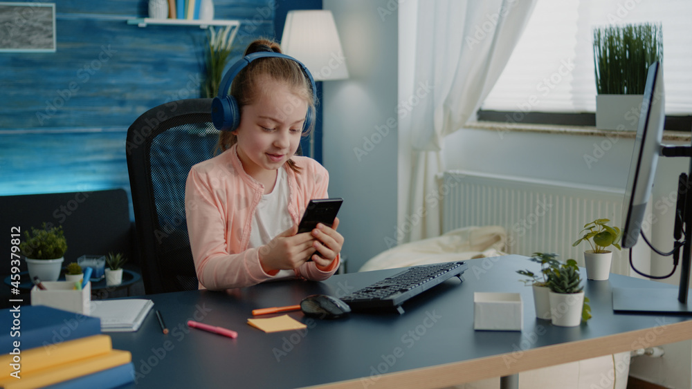 Little girl using smartphone for lessons on video call at desk. Young ...