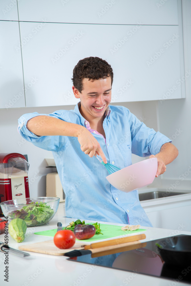 hombre joven sonriente batiendo huevos en bol rosa con camisa azul, men ...