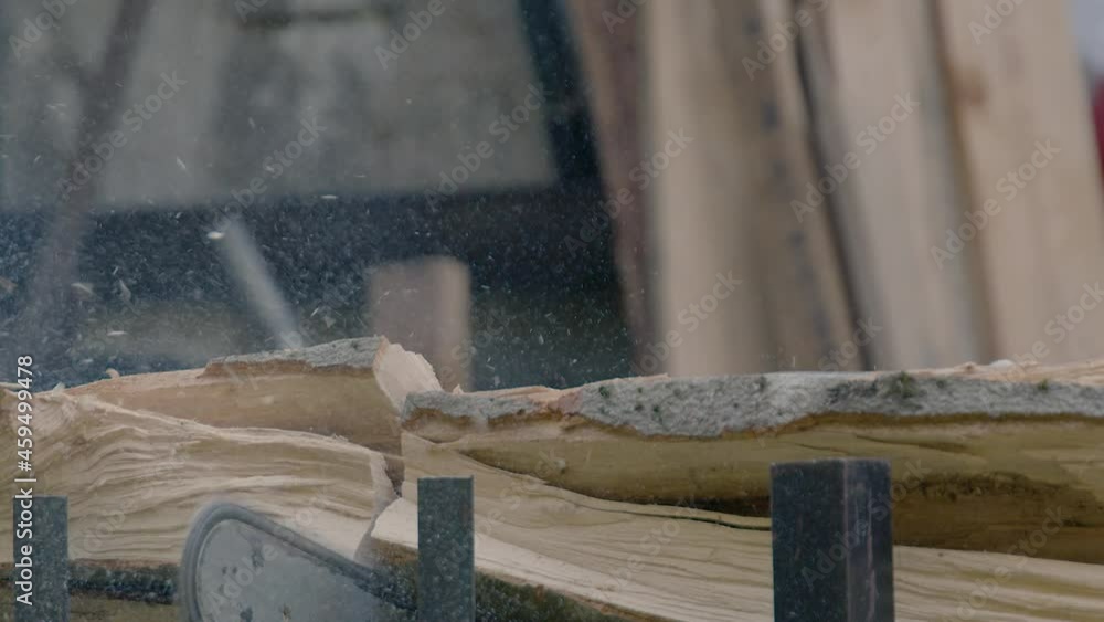 Cutting through wood with chainsaw. Firewood is stacked in an iron ...