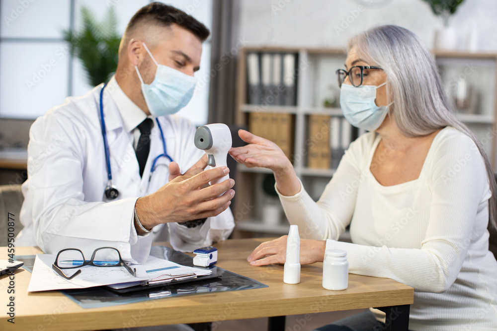 Male physician in face mask and lab coat using electronic contact less ...