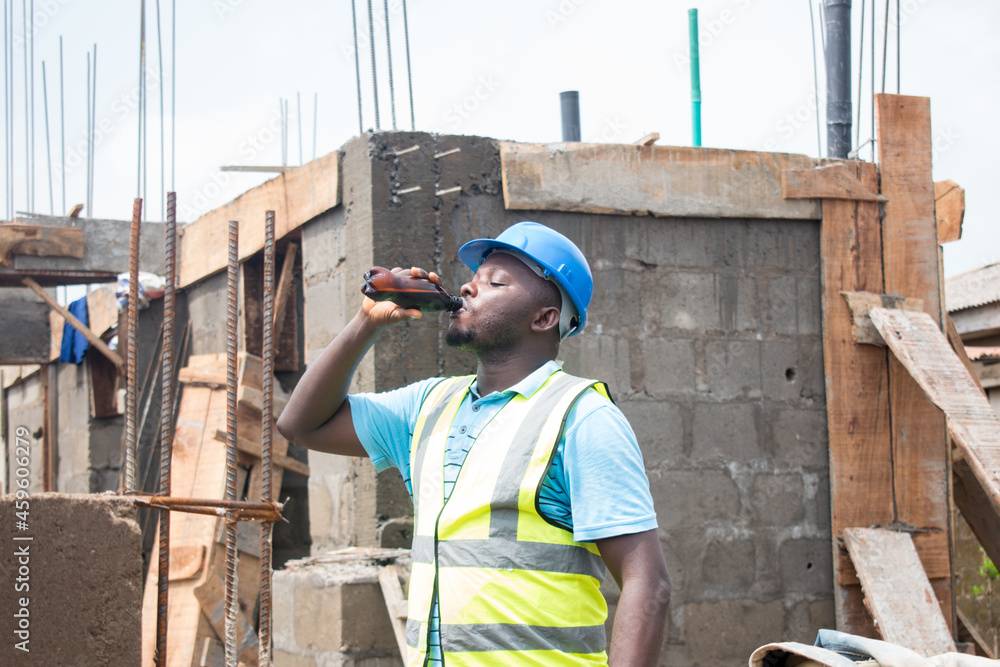 A thirsty male African construction worker drinking from a bottle on a ...