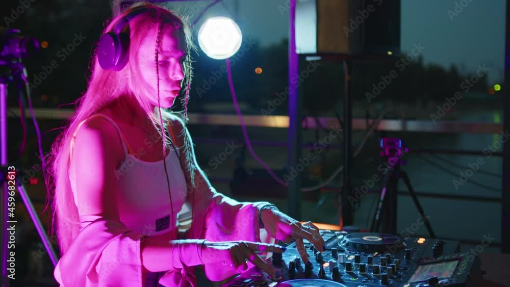 Cool dj is working in a nightclub, standing at turntables, creating a ...