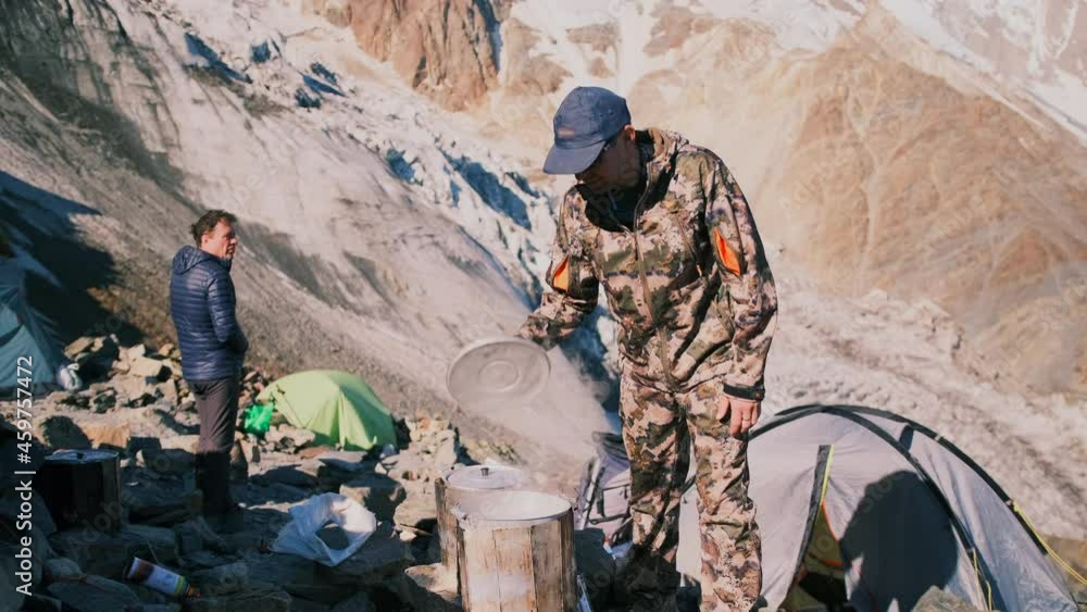 A man opens a lid of boiling cooked food in a saucepan at a mountain ...
