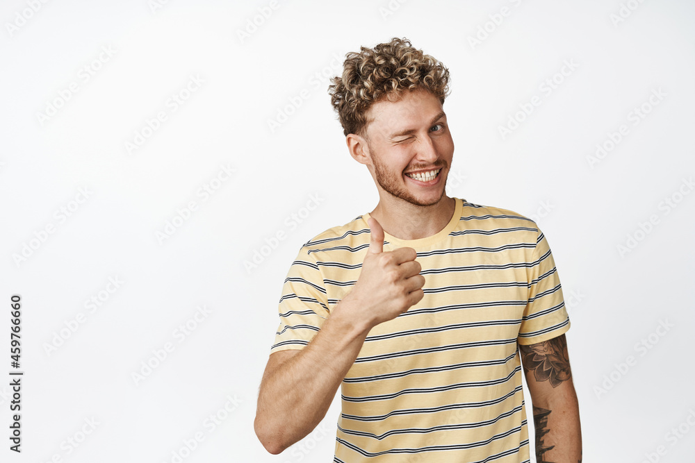 Handsome blond man winks and smiles, shows thumbs up in approval ...