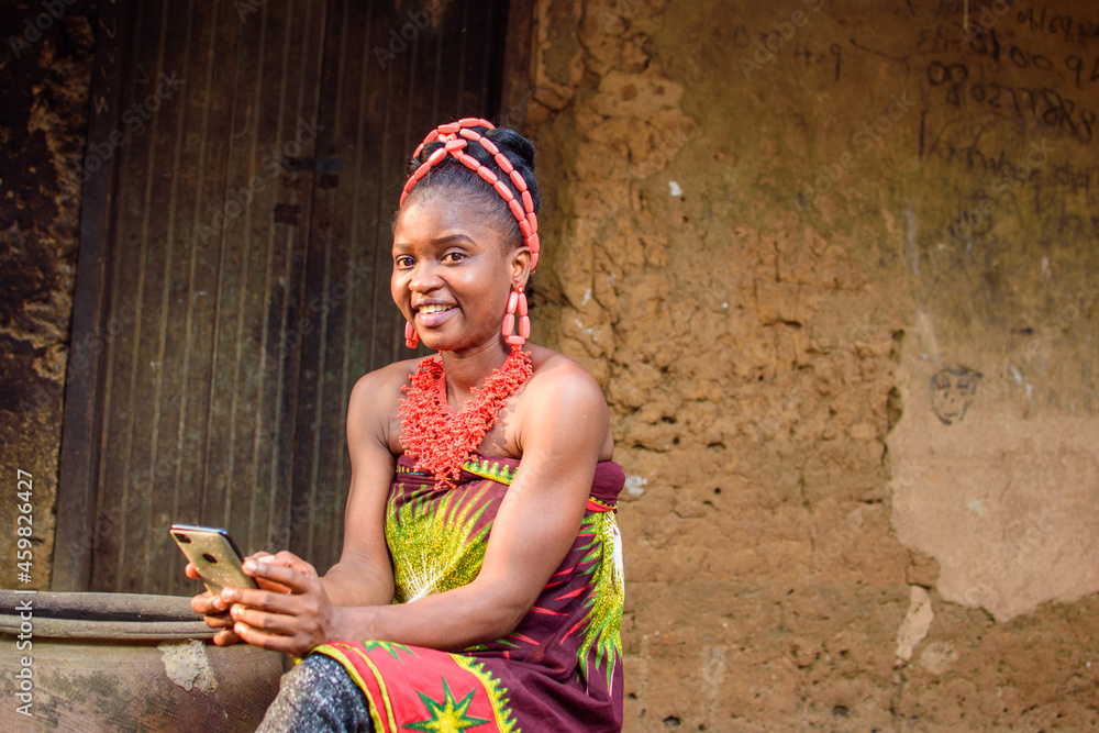 A happy African lady or woman with beads on her head, sitting beside ...