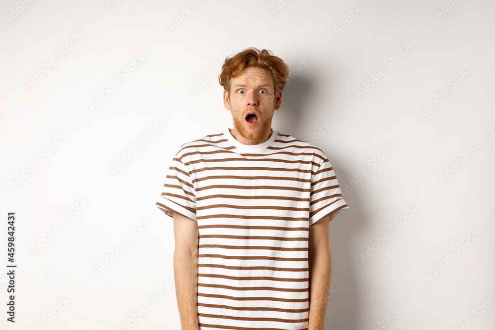 Shocked and scared redhead man screaming, open mouth and staring ...