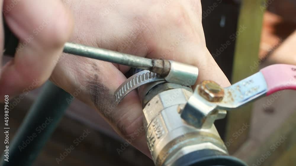 Close-up of a plumber installs a hose clamp on a flexible hose while ...