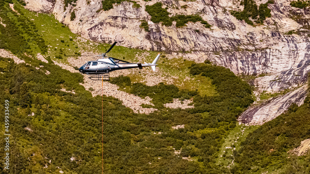 Beautiful alpine summer view with a helicopter in action, transporting ...