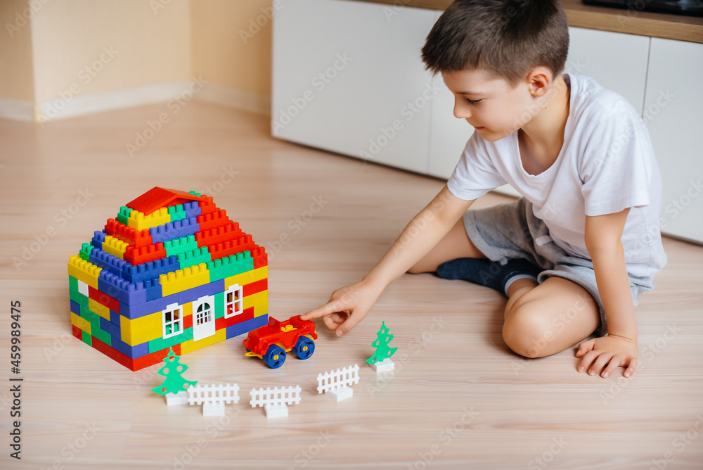 A little boy plays with a construction kit and builds a big house for ...