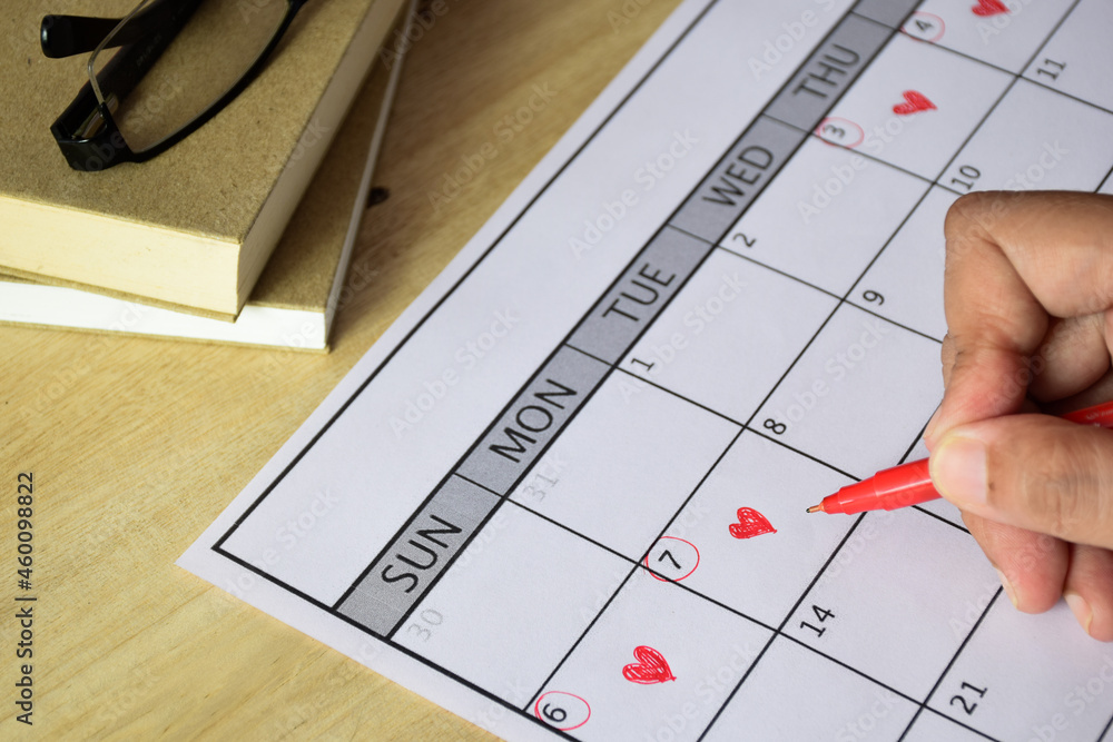 Woman hand marking her menstrual period days in calendar with red pen ...
