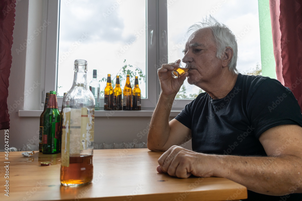 old senior male man sit next to table drink alcohol bottle at home sad ...