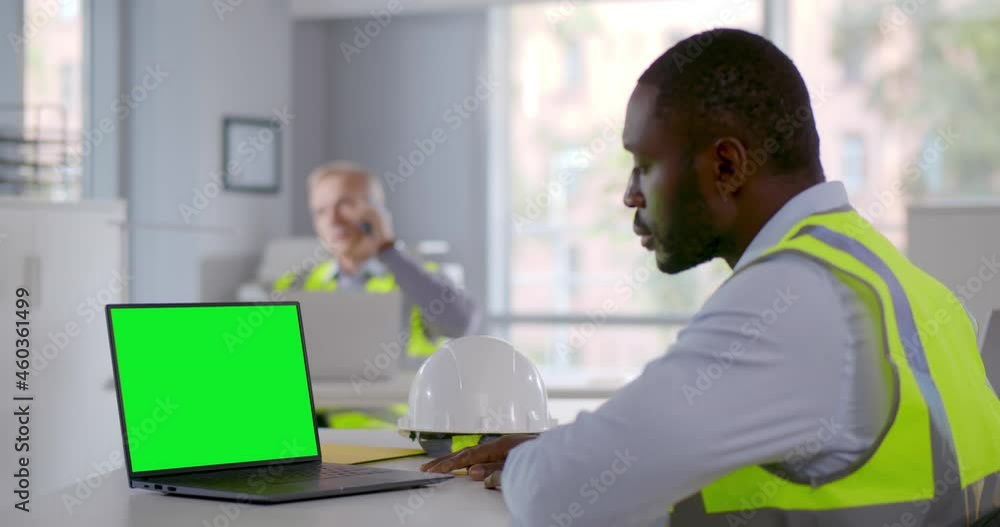 Side view of mixed-race engineer in reflective vest looking at laptop ...