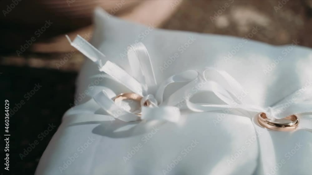Two golden wedding rings on small white lace pillow tied with ribbons ...