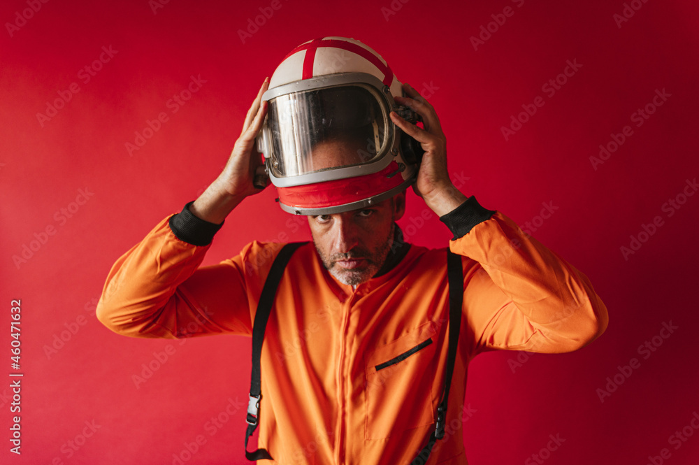 Astronaut with an orange space suit taking off his helmet on a red ...