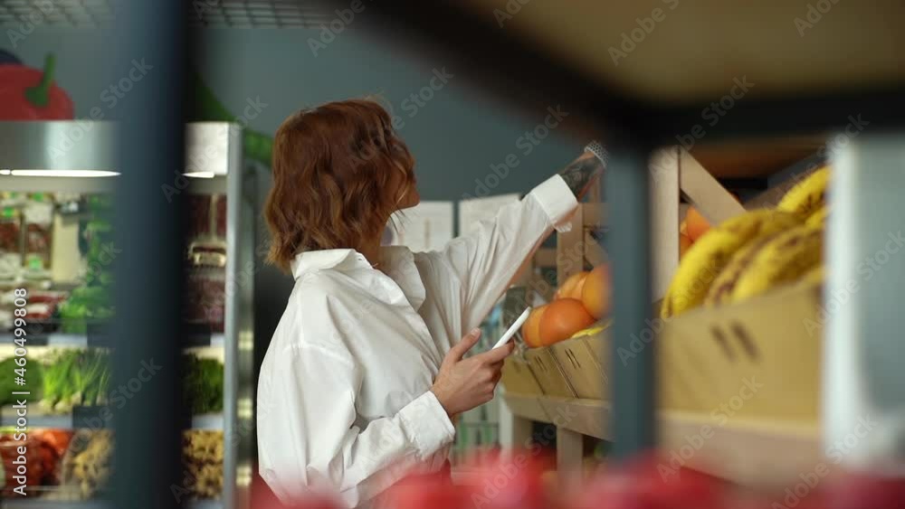 Female choosing products in market walking along counters taking photos ...