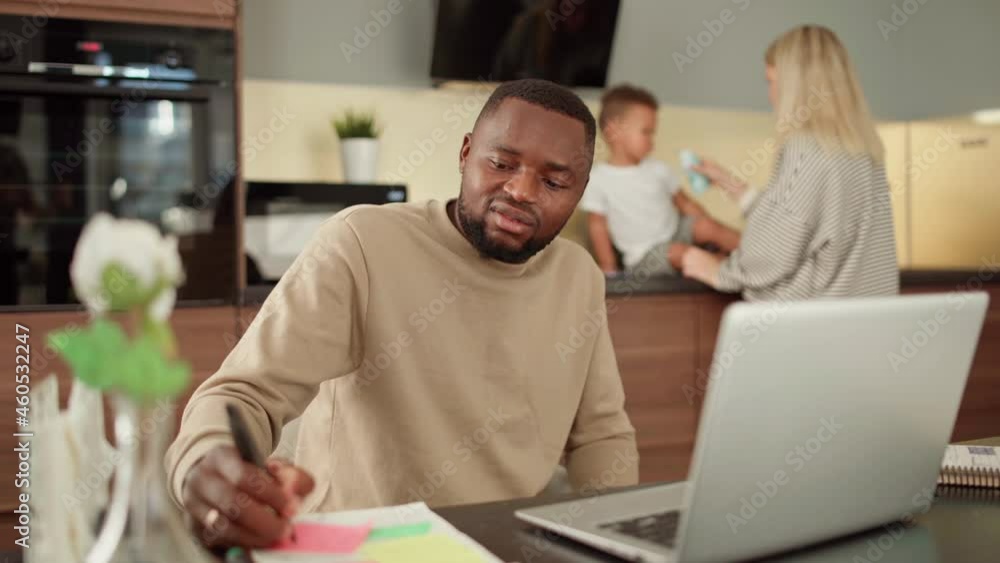 Black man working on laptop from home and making notes in notepad while ...