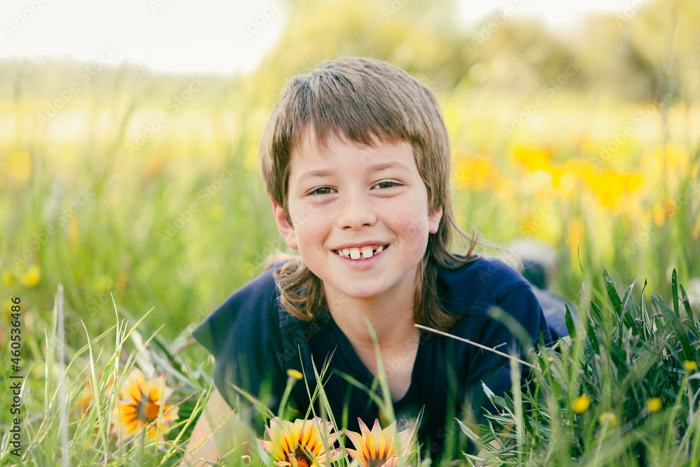 Plakát Boy with mullet hairstyle lying in long grass with wildflowers ...