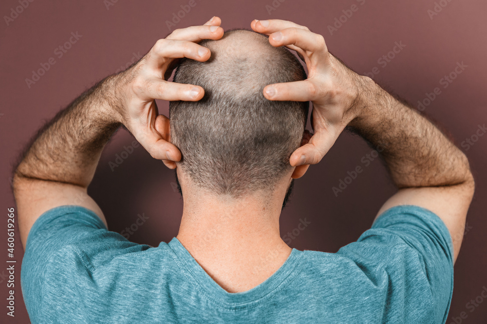 Baldy man grabs his head with his hands. Rear view. Brown background ...