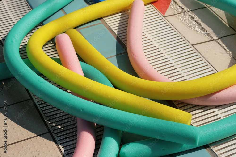 Multi-colored poolside noodles lit by the sun. The noodles are floating ...