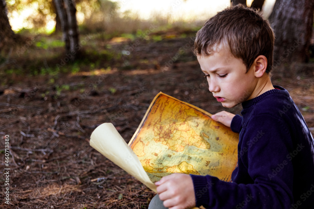 Boy trying to read an old travel map, lost in a forest, in search of ...