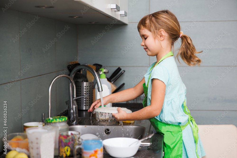 A little cute child girl washing dishes in the white kitchen interior ...