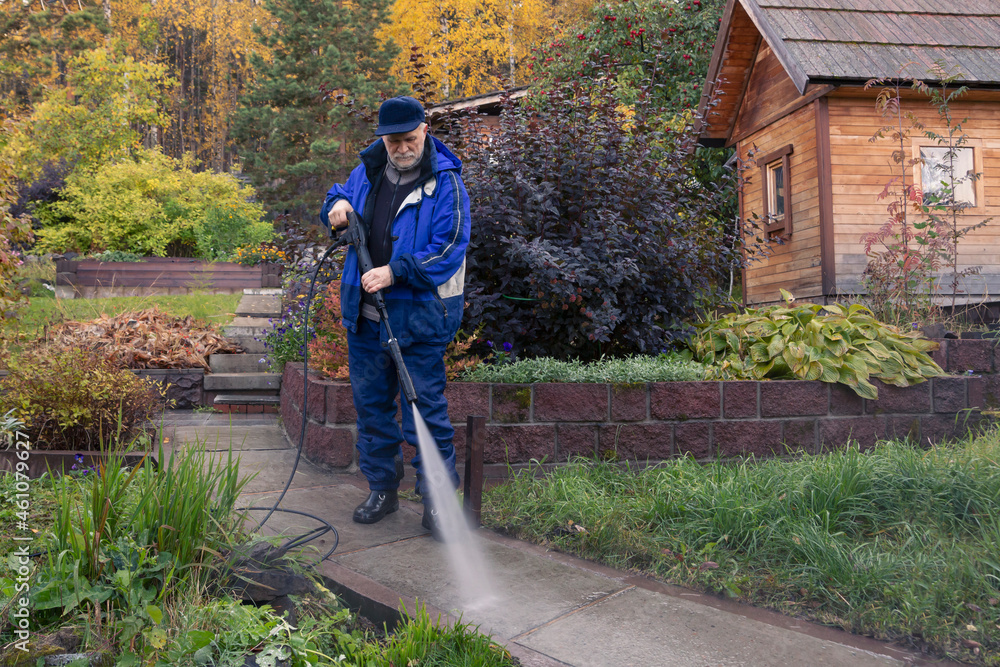 A man washes a garden path with a high pressure washer. Autumn work in ...