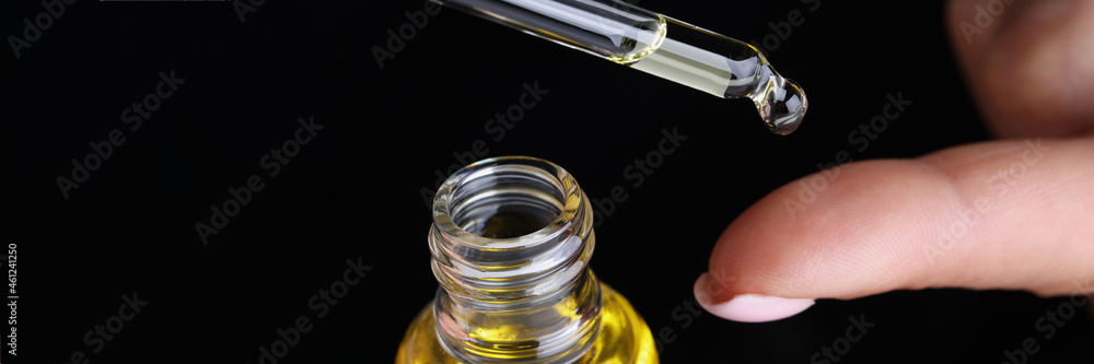 Drop of yellow oil flowing from dropper onto woman finger on black ...