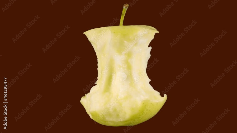 Bitten off ripe yellow apple, core, rotates on a brown background ...