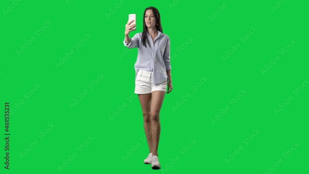 Pretty woman in smart casual summer clothes walking and taking selfie ...