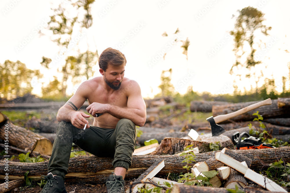Bearded young lumberjack wood worker sit smoking cigarette, having rest ...