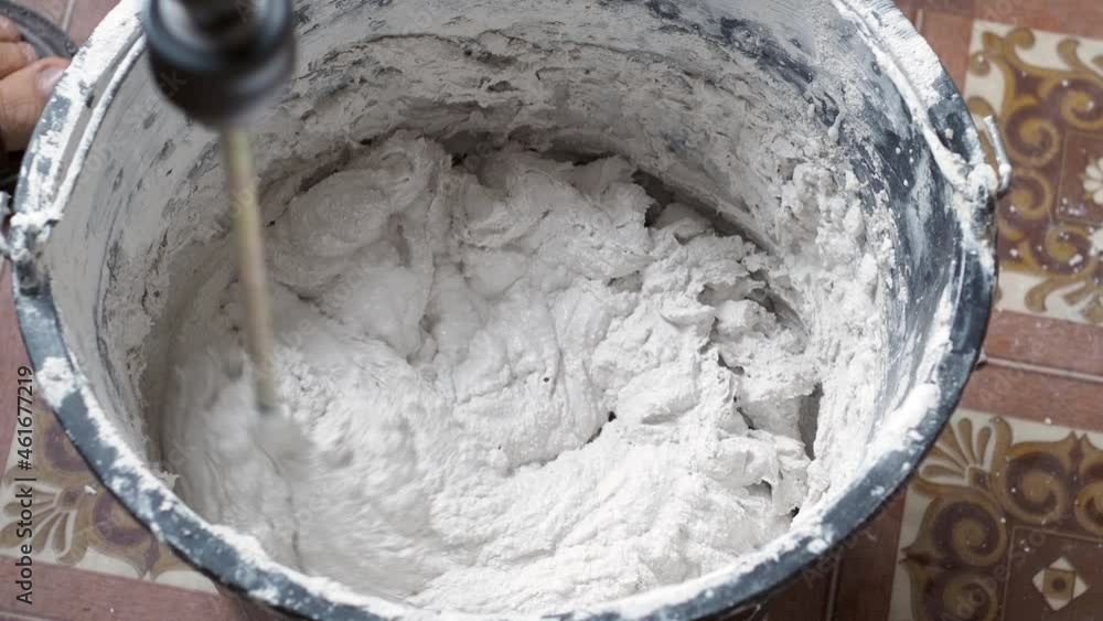 A person mixes cement and water in a container to get the finished ...