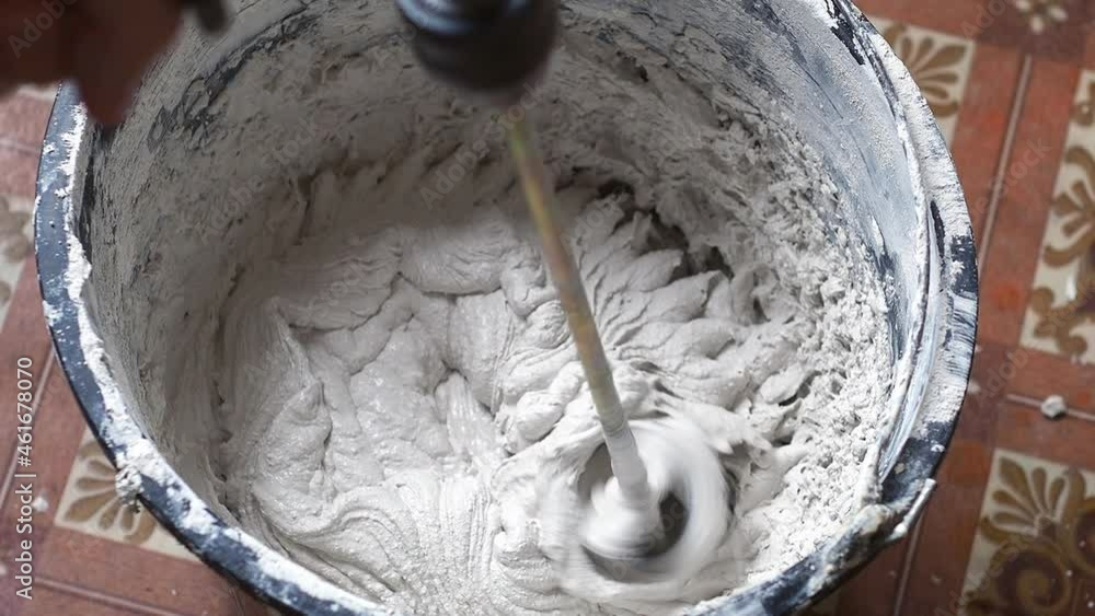 A person mixes cement and water in a container to get the finished ...