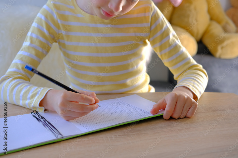 child, schoolboy in yellow t-shirt, writes letters in notebook with an ...