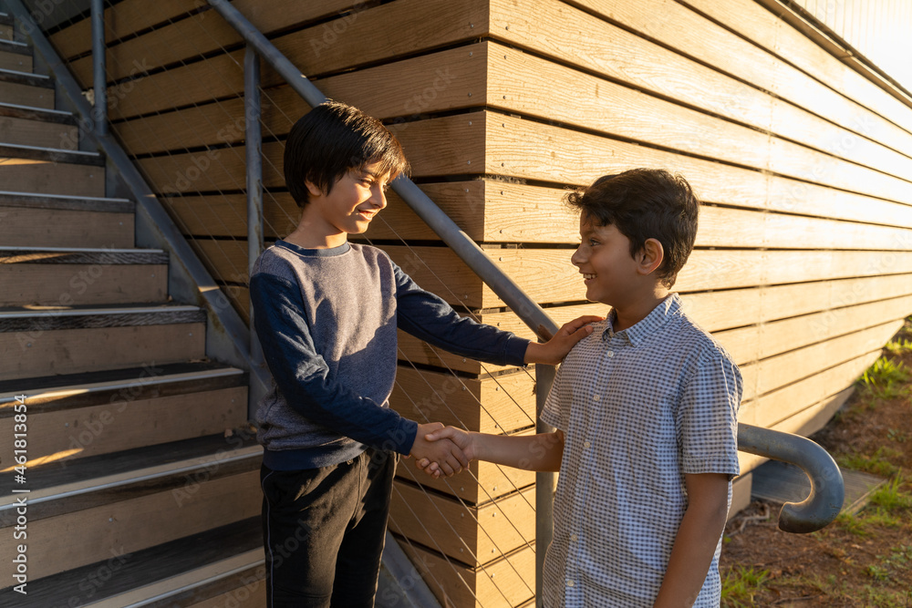 Two smiling young boys shaking hands standing on stairs. Hand on ...