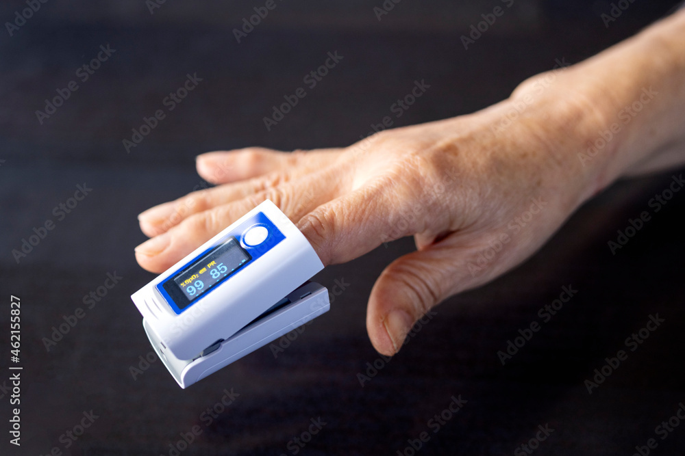 Elderly person's finger and pulse oximeter seen from an angle, black ...