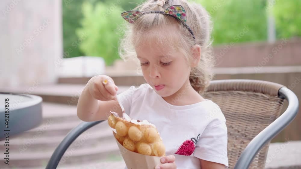Little girl eat bubble waffle with ice cream sitting outdoor cafe ...