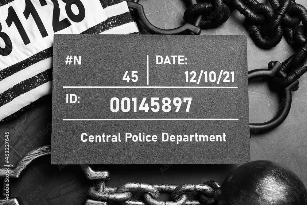 Metal ball with chain, prison uniform and mugshot letter board on grey ...
