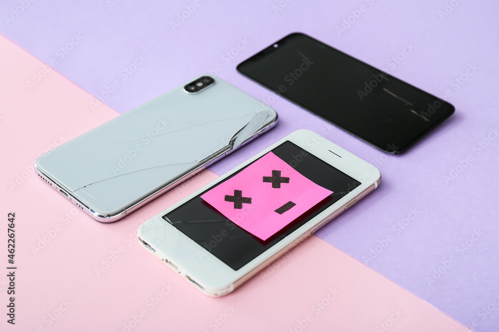 Damaged mobile phones, display glass and sad smile on color background ...
