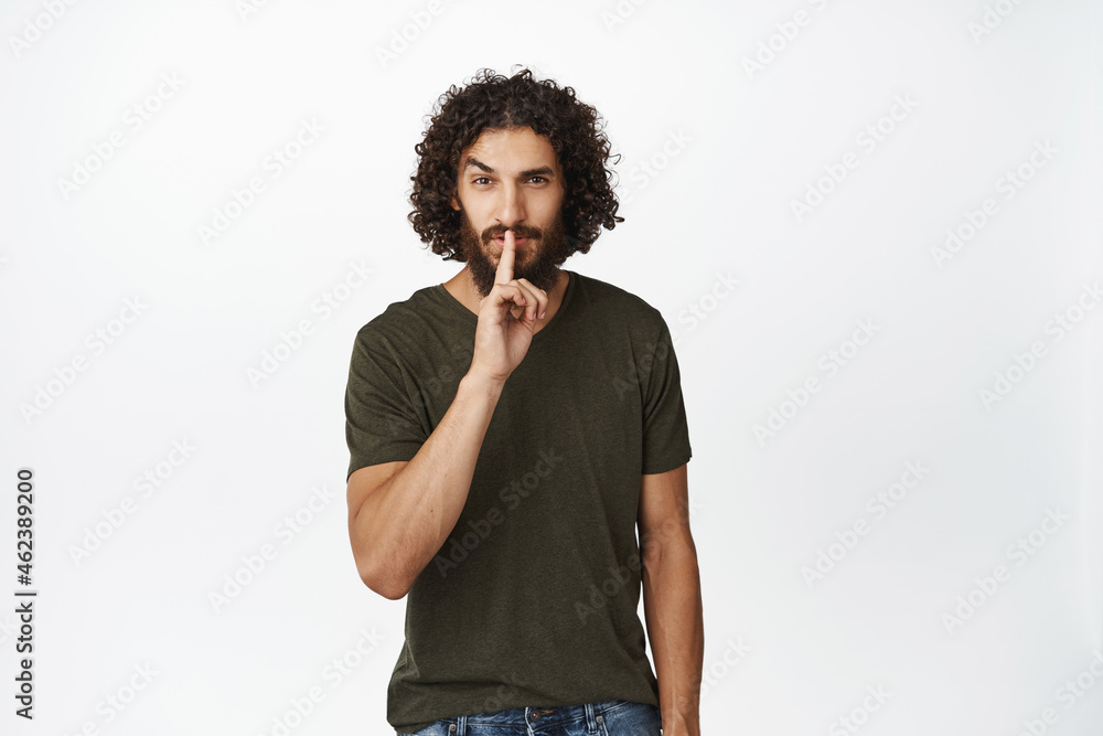 Young middle-eastern guy shushing, making hush sign with finger on lips ...