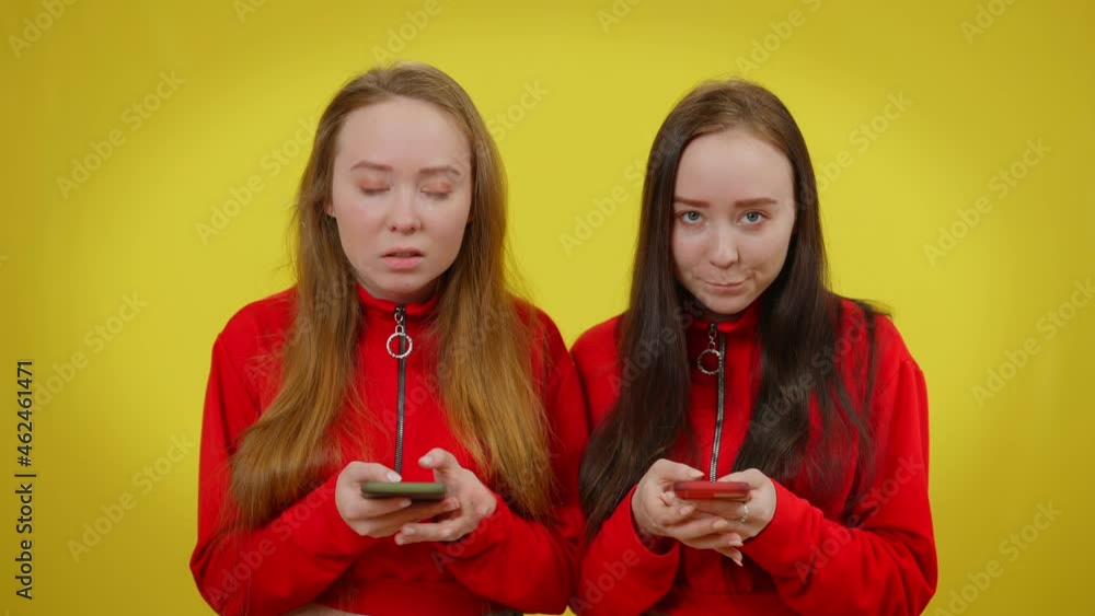 Absorbed twin sisters texting fast on smartphones looking at camera ...