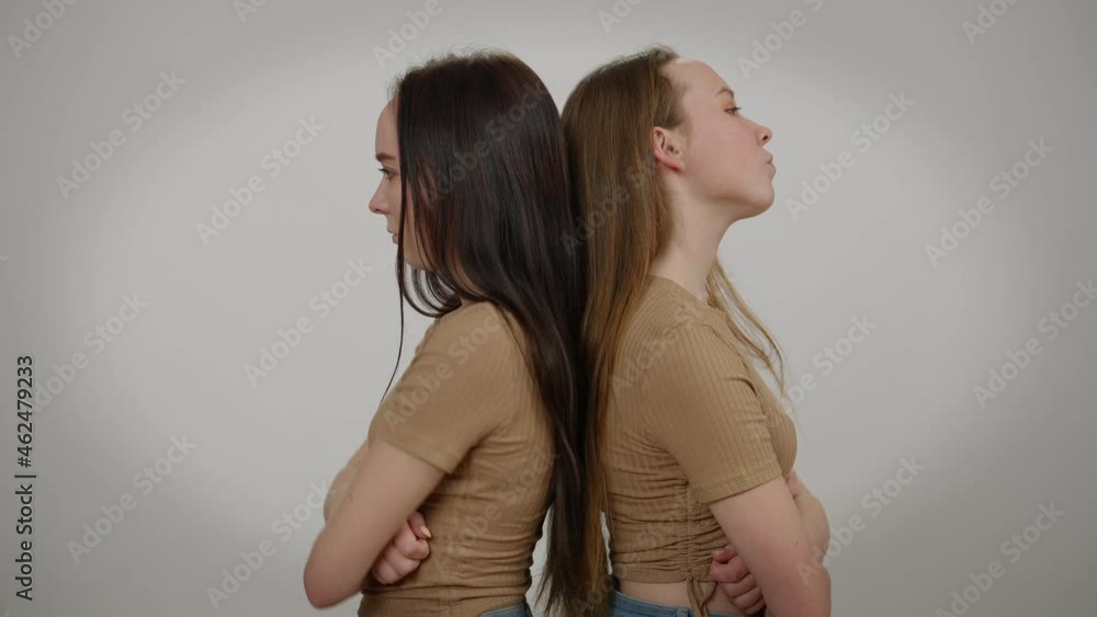 Side view slim young beautiful women standing back to back at grey ...