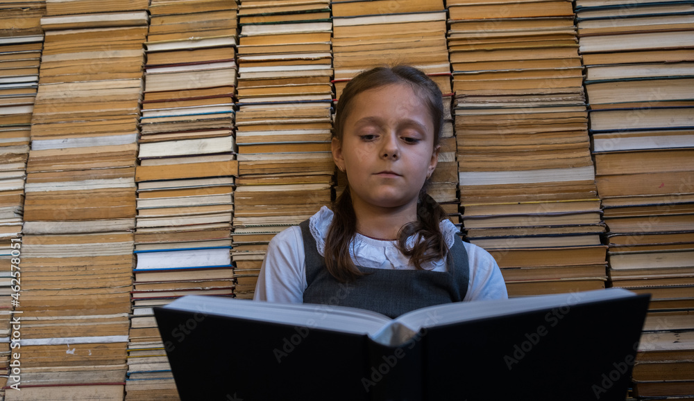 Curious cute preschool kid girl sitting with a book, on books ...