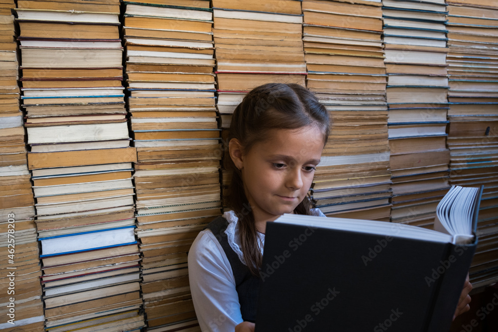 Curious cute preschool kid girl sitting with a book, on books ...