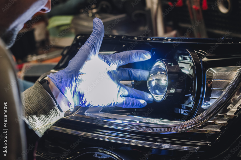 Car headlight in repair close-up.An auto mechanic wearing gloves checks ...