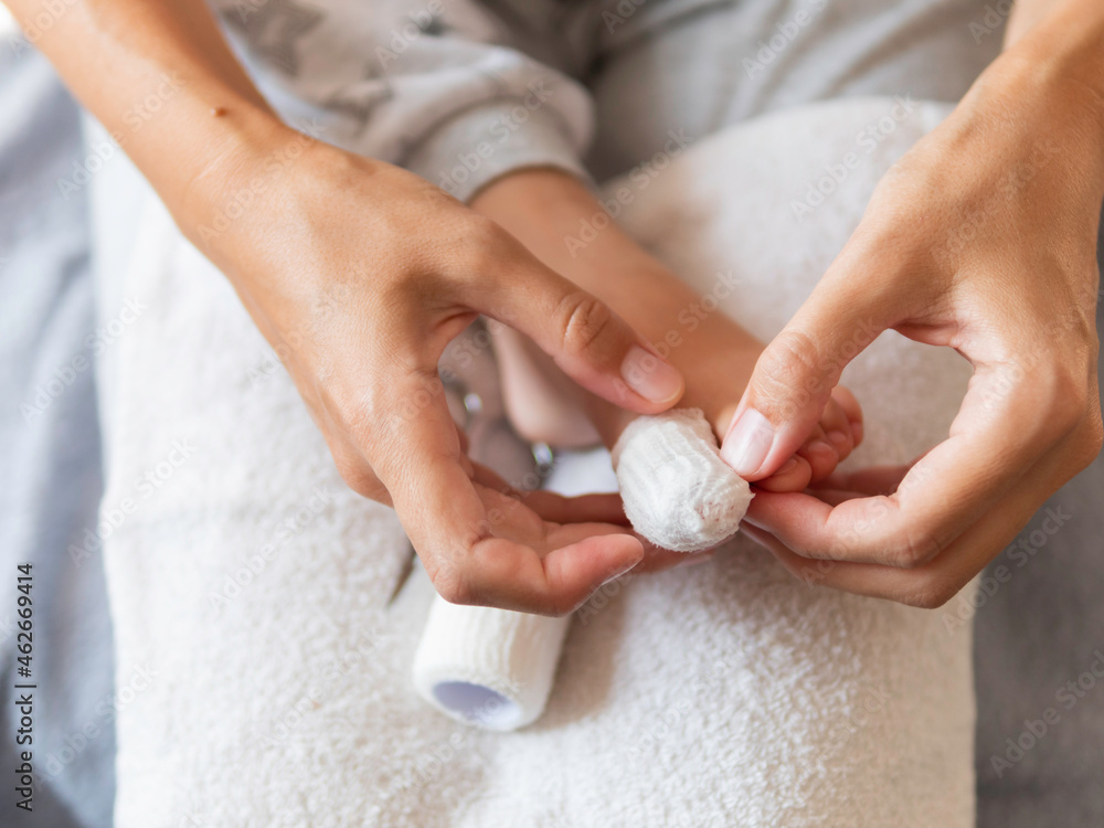 Mother bandages her child's big toe. Close-up photo of kid's foot with ...