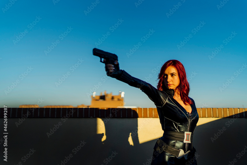 Portrait of redheaded woman with gun in her hand wearing black leather ...